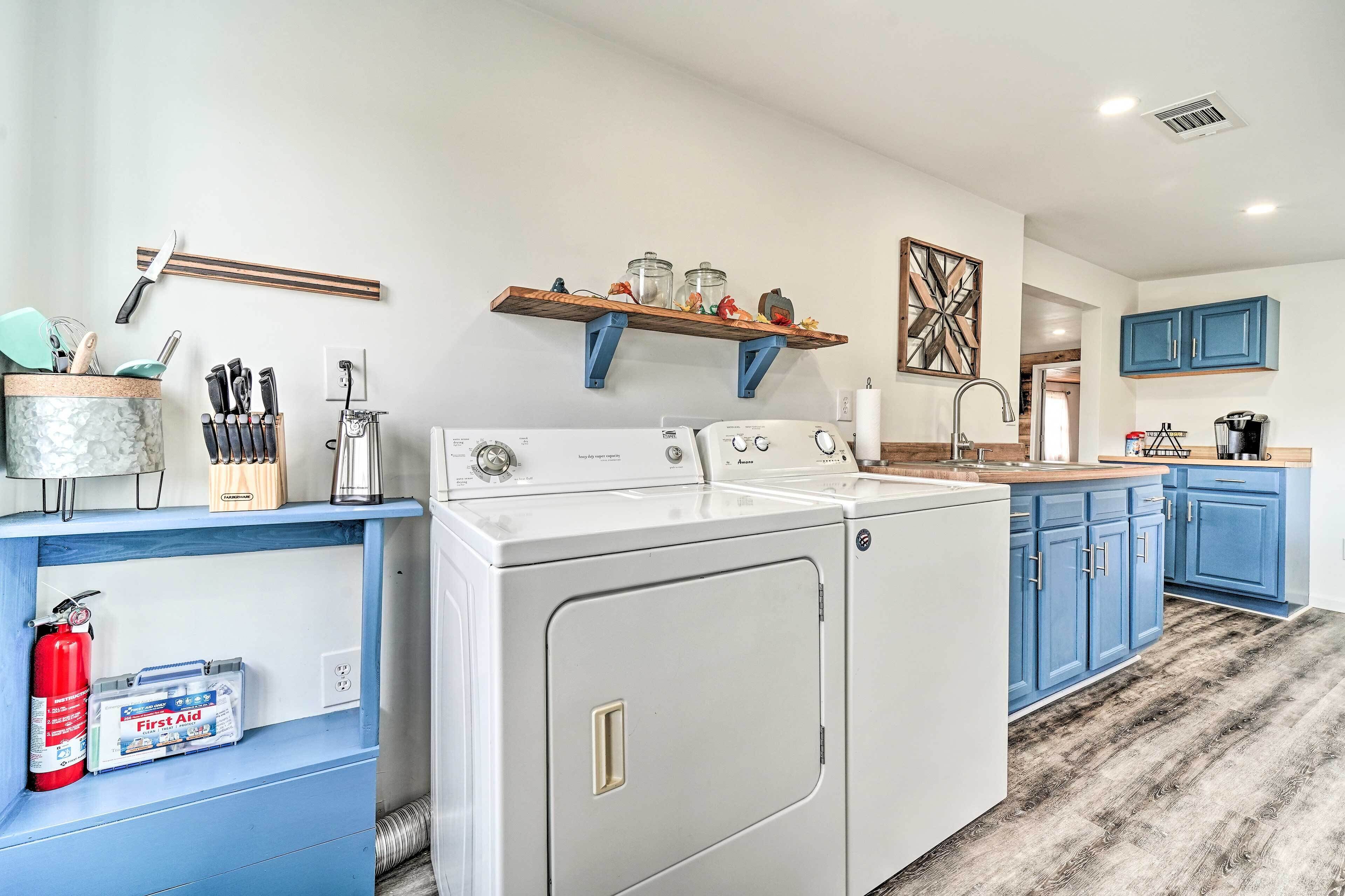 Cozinha moderna com máquina de lavar e secar integradas, armários azuis e prateleira de madeira com objetos decorativos.