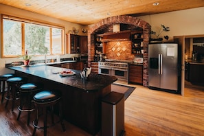 Uma cozinha com uma ilha grande, banquetas, geladeira e painel de backsplash de tijolos.