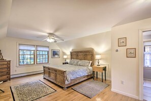 Quarto com cama de madeira, duas mesas de cabeceira com abajures, ventilador de teto e uma grande janela com persianas.