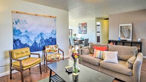 Sala de estar com uma grande pintura abstrata, um sofá, uma poltrona e uma mesa de centro com um vaso de flores.
