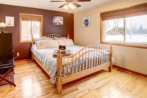Quarto com cama de madeira, ventilador de teto e janela com vista para uma paisagem nevada.