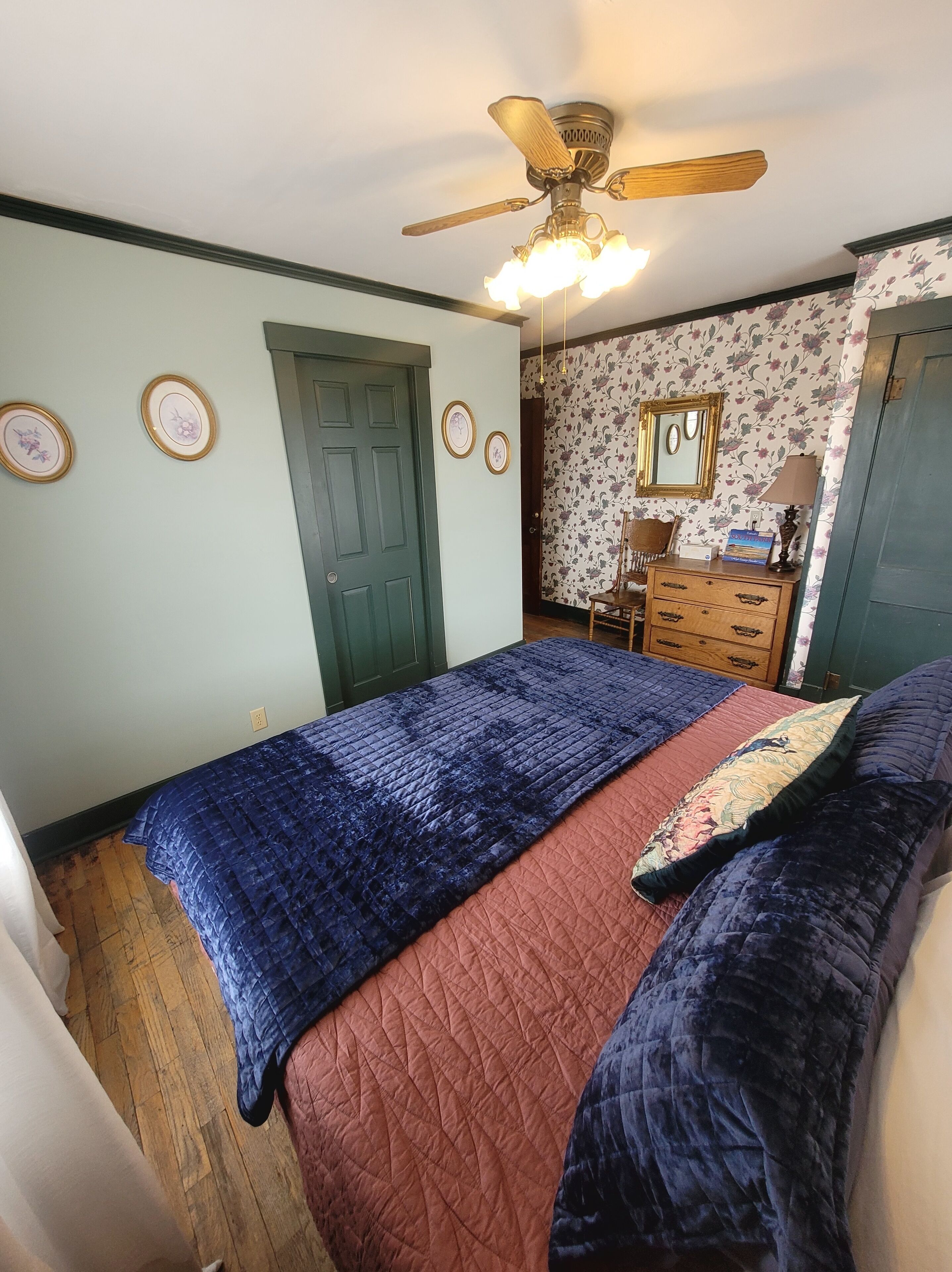 Quarto com cama, cômoda, espelho e ventilador de teto.