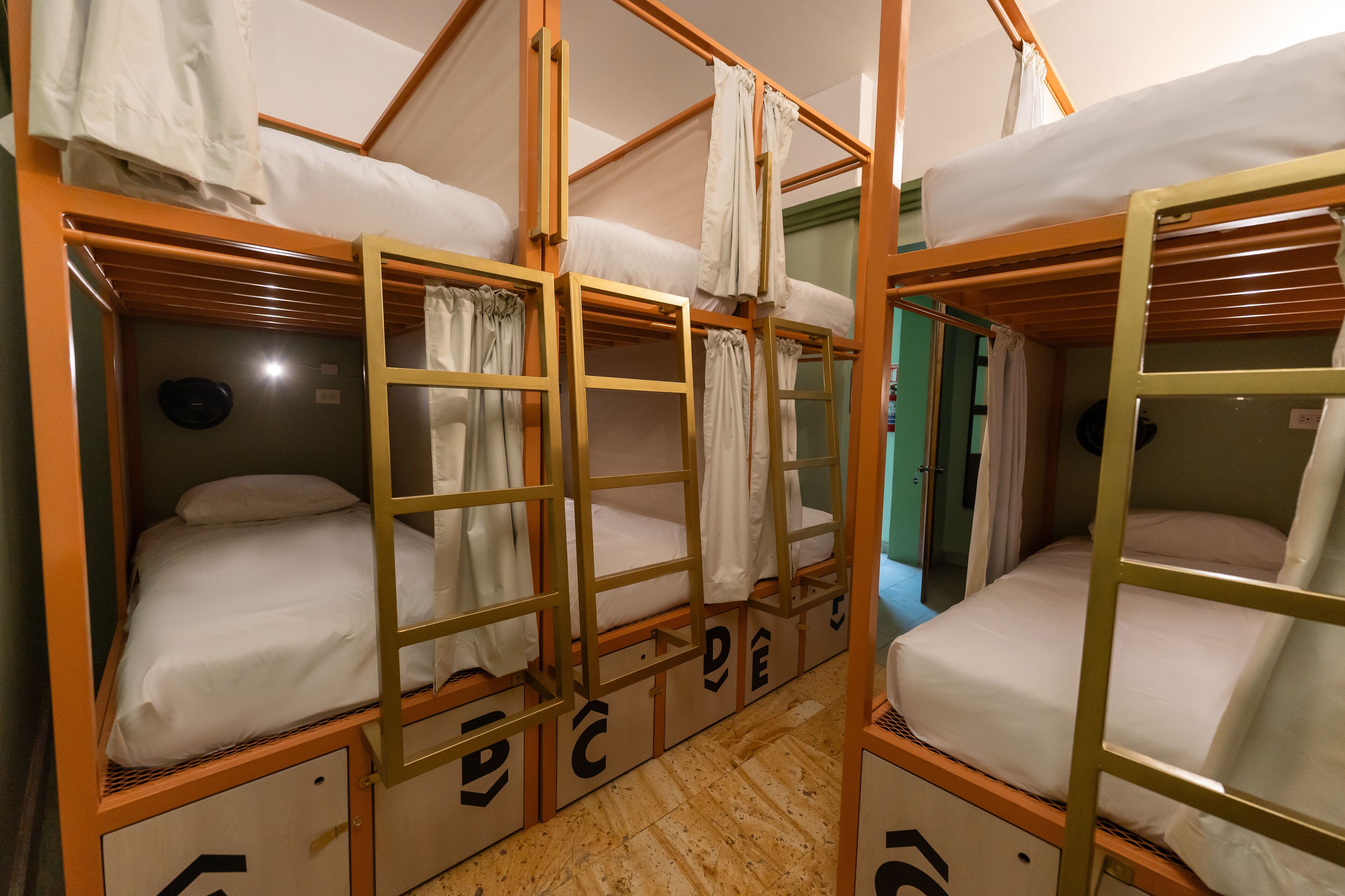 Quarto em estilo de dormitório, com beliches, estrutura de madeira e roupa de cama branca.