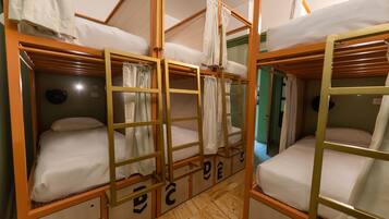 Quarto em estilo de dormitório, com beliches, estrutura de madeira e roupa de cama branca.