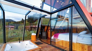 Um espaço moderno envidraçado com deck de madeira, uma banheira grande e uma cama com roupa de cama branca.