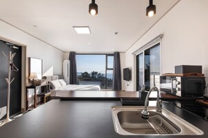Quarto de hotel moderno com uma cama grande, cozinha compacta, pia e vista para o exterior.