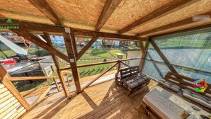 Um deck de madeira com vista para uma aldeia, um banco e uma mesa com almofadas.