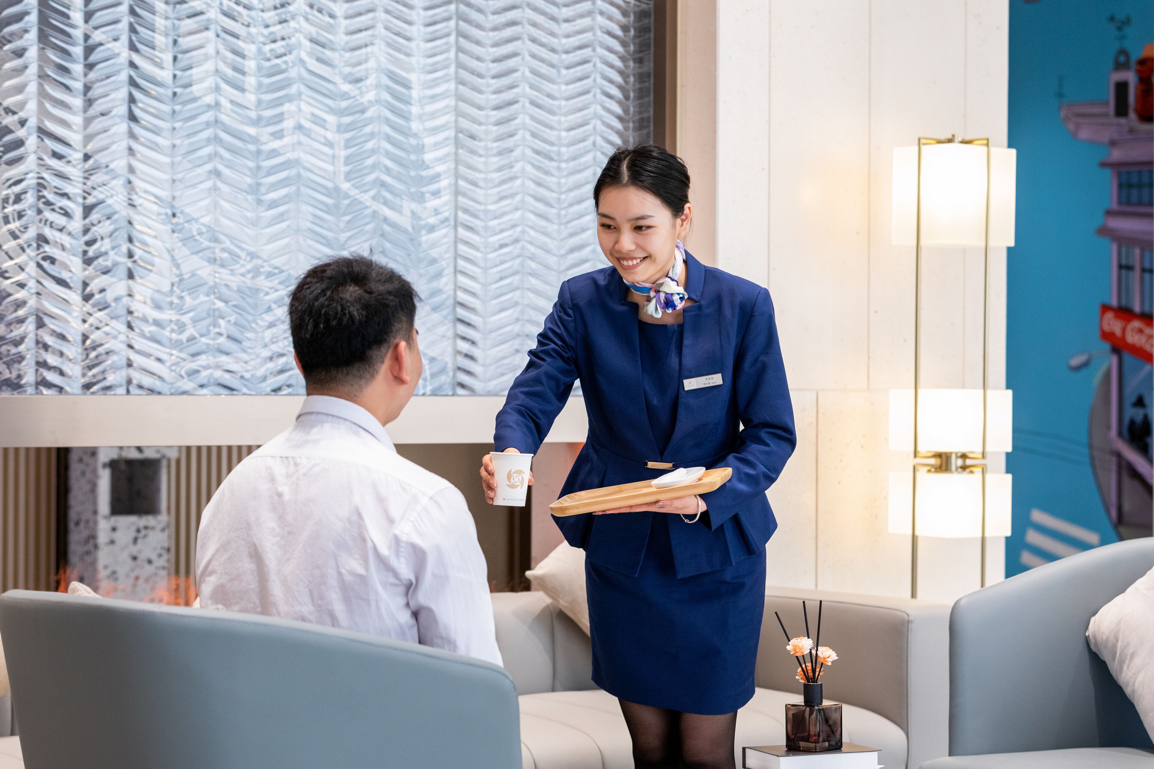 Um hall de hotel com design moderno, apresentando uma mesa de recepção, área de estar e painéis decorativos na parede.