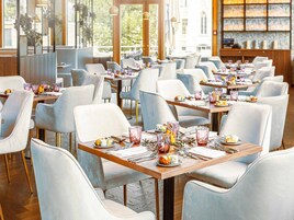 Um restaurante com várias mesas e cadeiras, cada conjunto com pratos, copos e talheres.