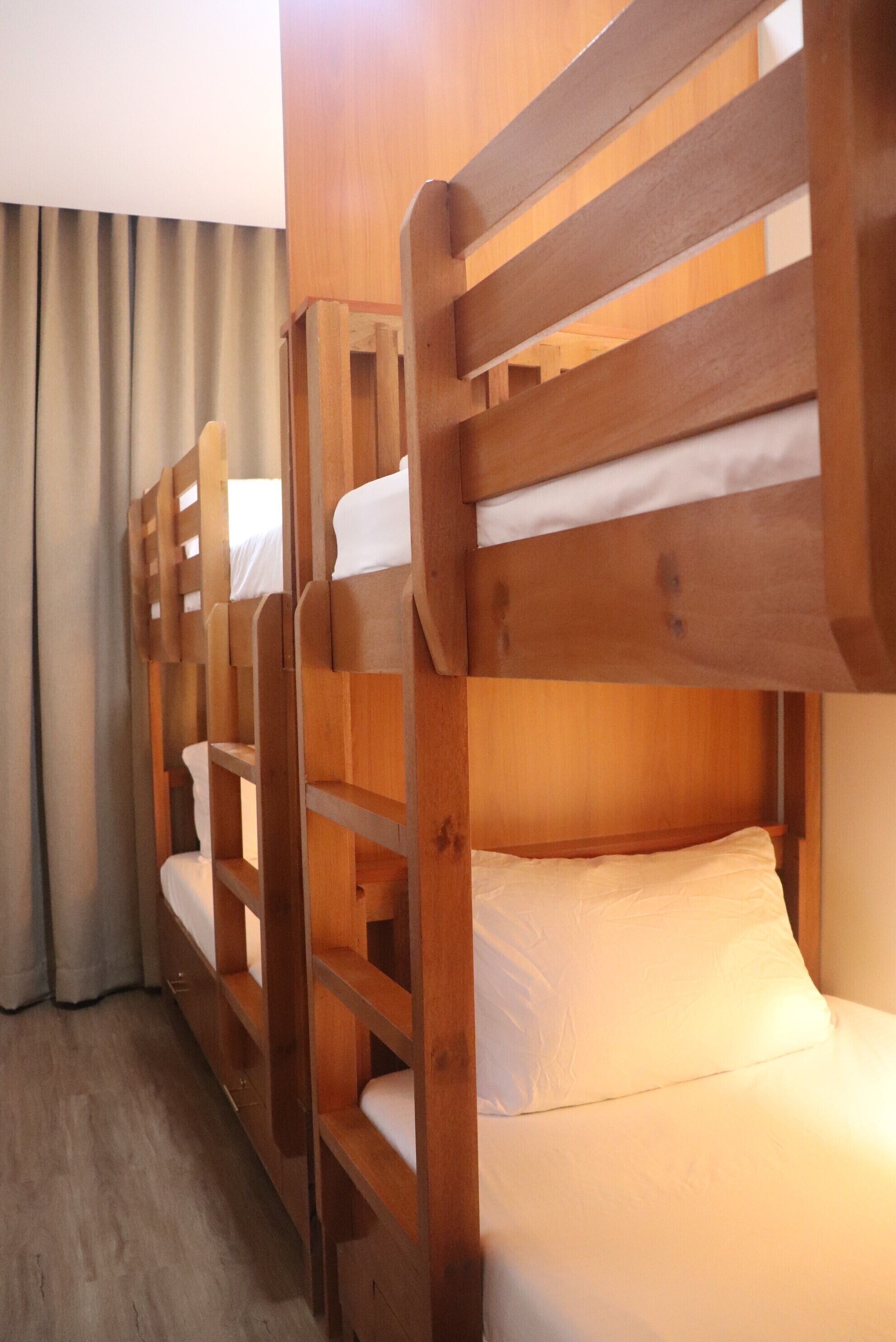 Quarto com beliches de madeira, cortina e chão de madeira.