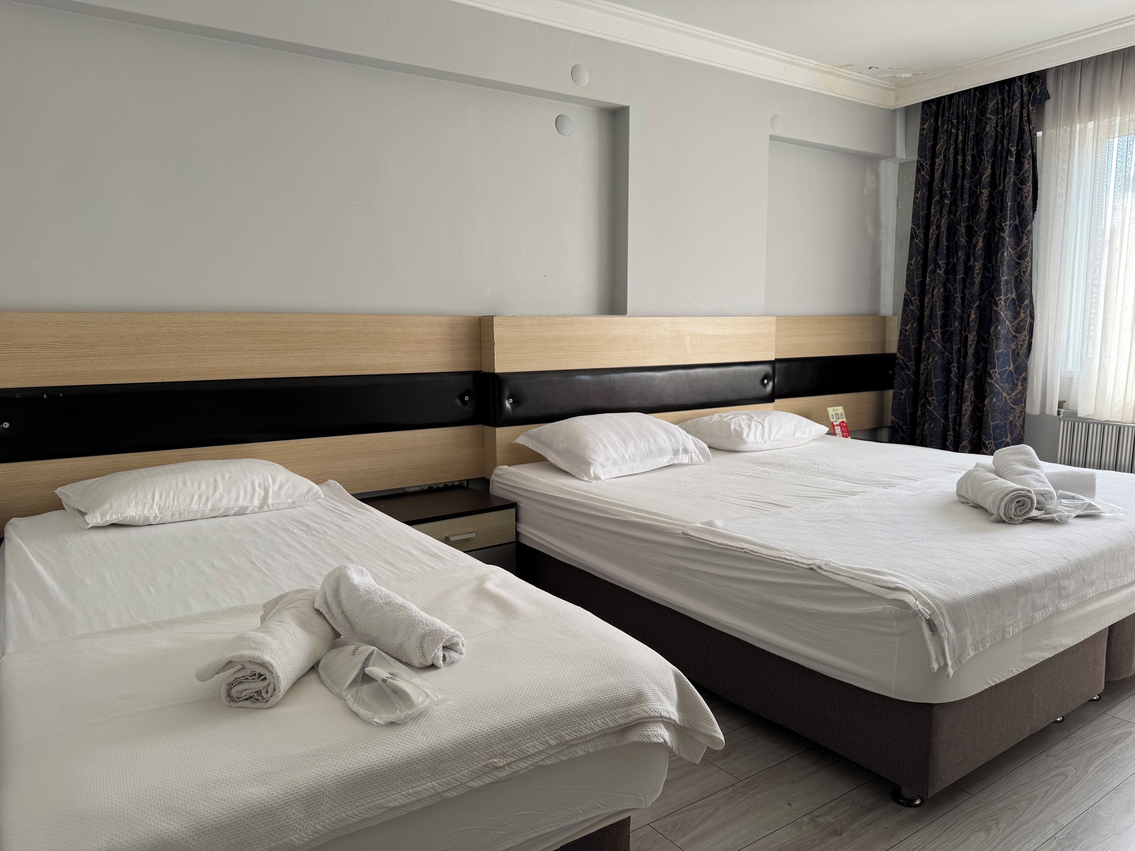 Quarto de hotel com duas camas, cada uma com roupa de cama e almofadas brancas, cabeceira de madeira e uma pequena mesa de cabeceira.