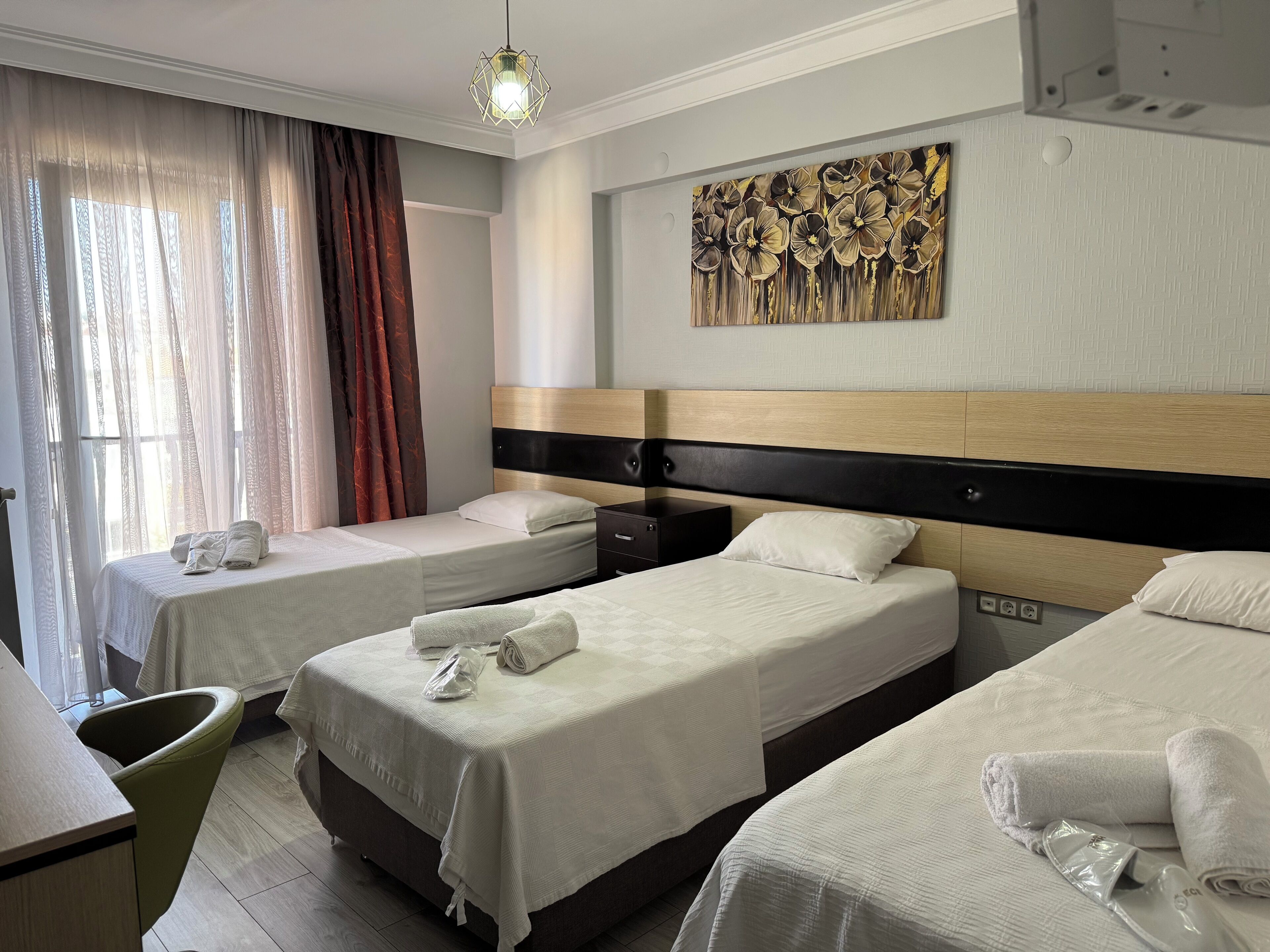 Quarto de hotel com três camas, uma escrivaninha e um quadro na parede.