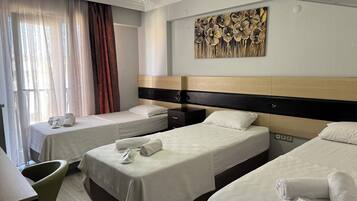 Quarto de hotel com três camas, uma escrivaninha e um quadro na parede.