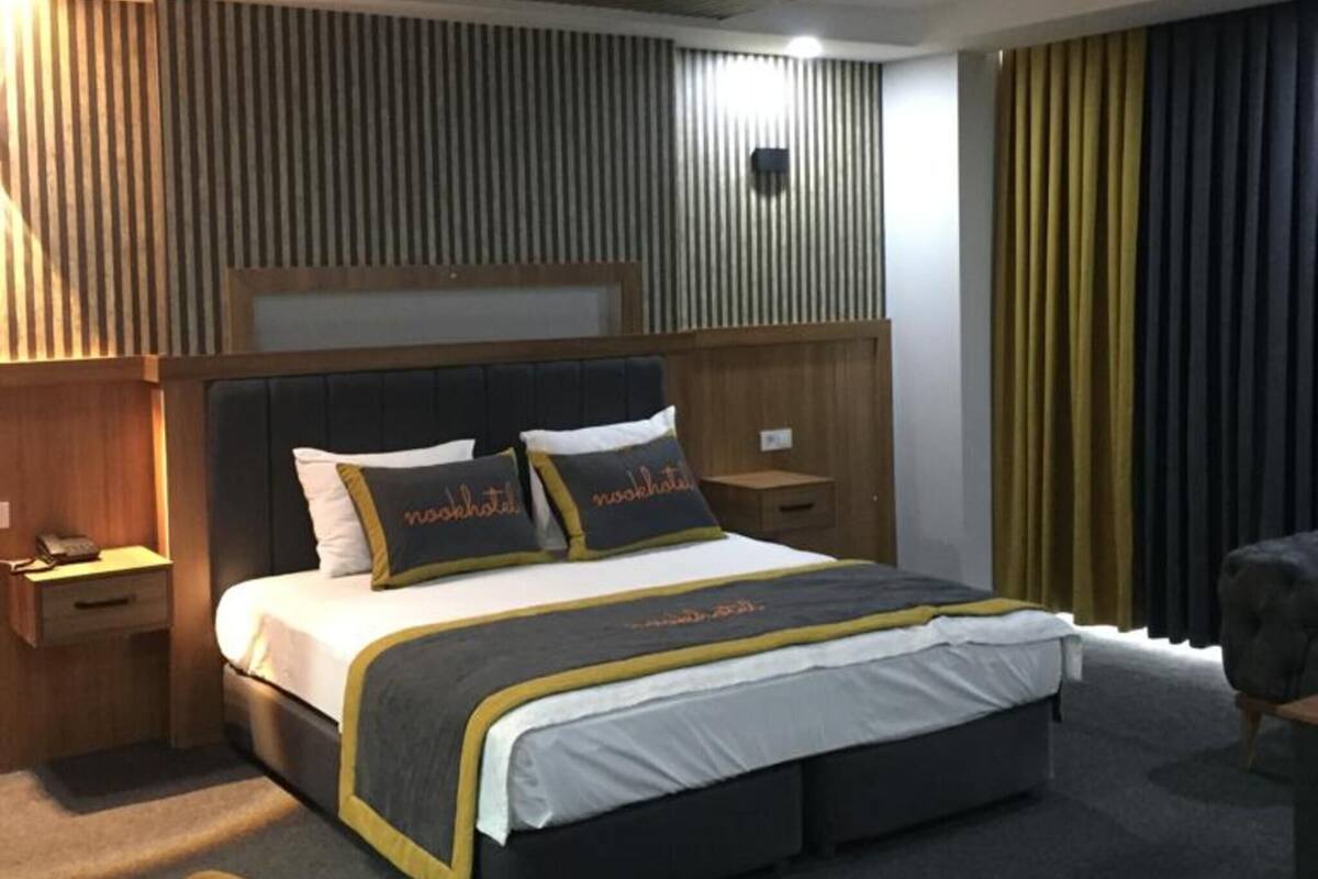 Quarto de hotel moderno com uma cama grande, uma mesinha de cabeceira, uma cadeira e um design de teto singular.