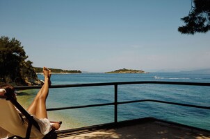 Uma pessoa relaxando numa varanda com vista para o mar e uma ilha ao longe.