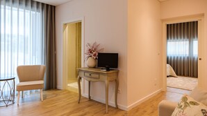 Uma sala de estar moderna com piso de madeira, um sofá bege, uma mesa redonda pequena e uma TV sobre um suporte de madeira.