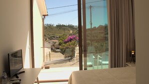 Quarto de hotel com varanda, uma cama, televisão e vista para a paisagem.
