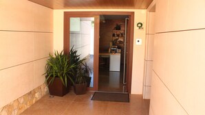 Um corredor com teto de madeira, piso de azulejos e uma porta que dá para um espaço com cozinha visível.