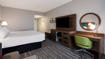 Quarto de hotel com cama, escrivaninha, cadeira, televisão e espelho.