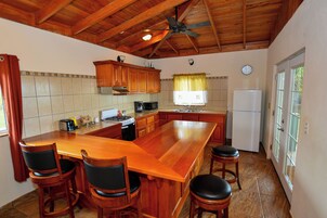Uma cozinha com armários de madeira, uma ilha central com banquetas e um ventilador de teto, além de uma geladeira.
