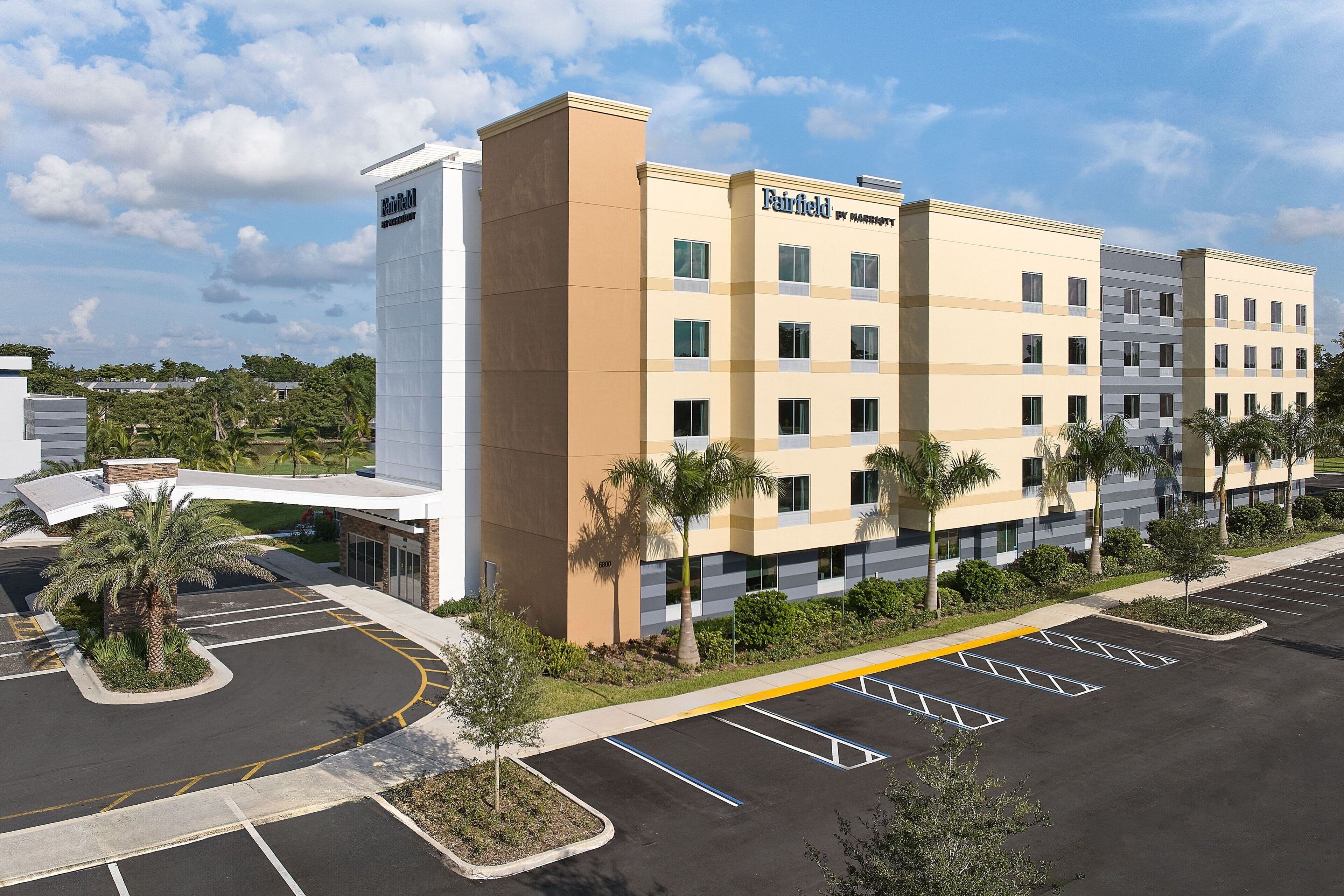 Um hotel Fairfield by Marriott com design moderno, apresentando um estacionamento com vagas demarcadas e palmeiras.