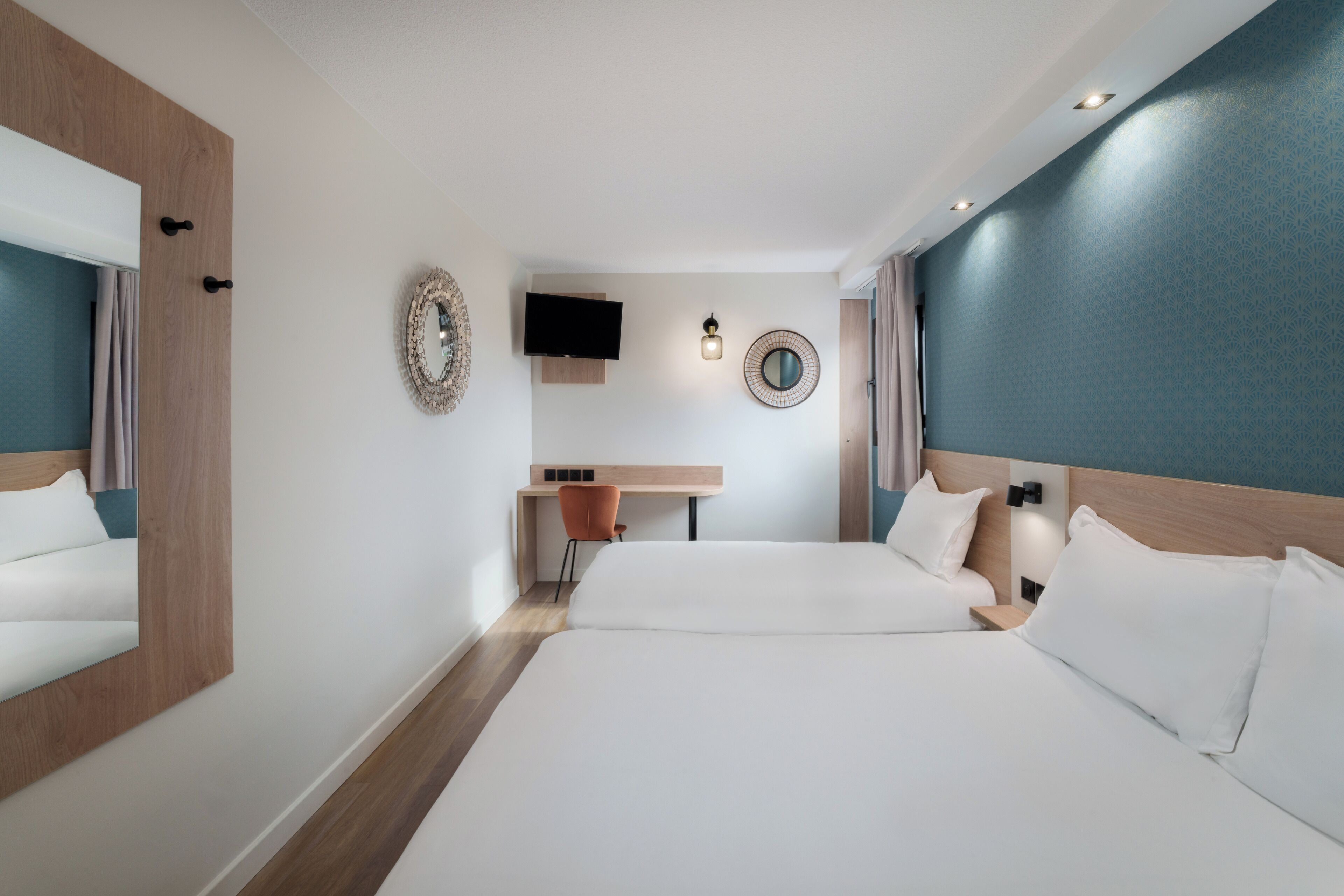 Quarto de hotel com duas camas, uma mesa, uma televisão e um espelho.