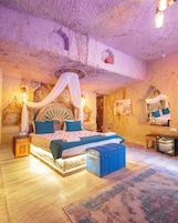 Quarto com cama de dossel, mesa de cabeceira, pequena mesa, cómoda azul e tapete estampado.