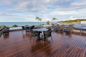Um deck de madeira com área de estar externa, piscina e vista para o oceano.
