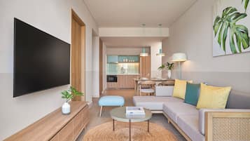 Uma sala de estar moderna com televisão de tela plana, sofá, mesa de centro e uma área de refeições ao fundo.
