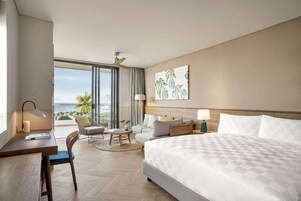 Quarto de hotel com uma cama grande, uma escrivaninha, uma cadeira, um sofá e vista para o oceano.
