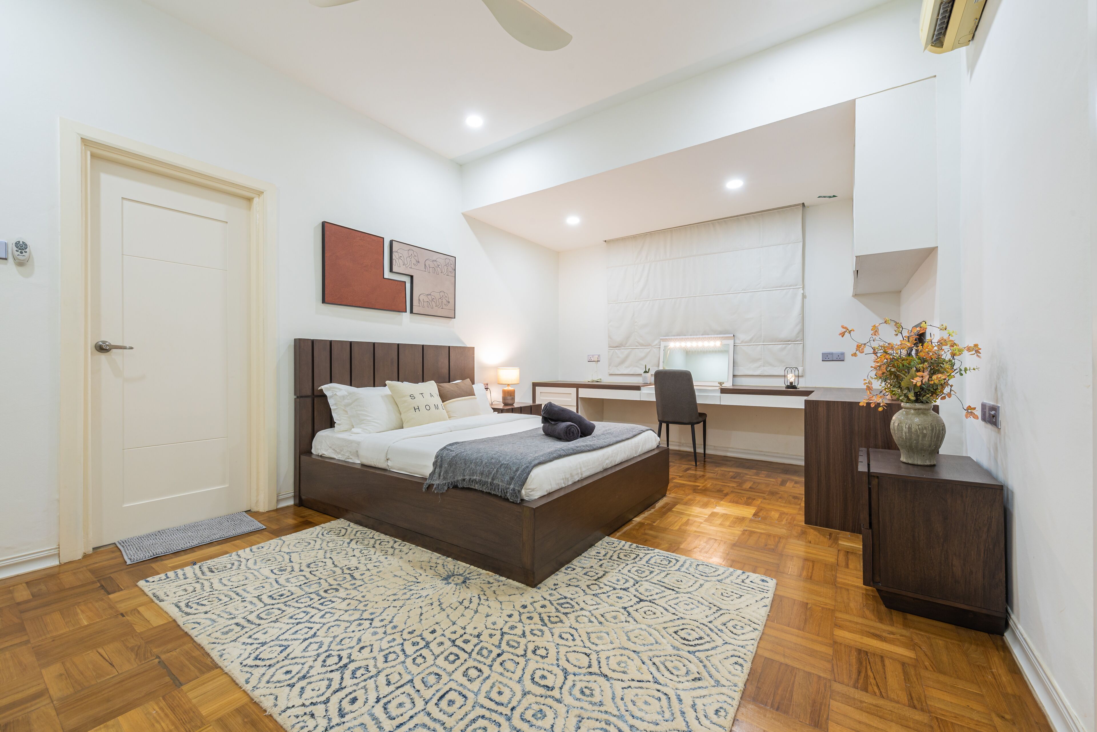 Um quarto com cama, escrivaninha e cadeira, um armário pequeno e um vaso decorativo.