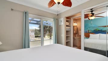 Quarto com cama grande, ventilador de teto, vista para o exterior através de uma porta deslizante e banheiro com chuveiro e vaso sanitário à vista.