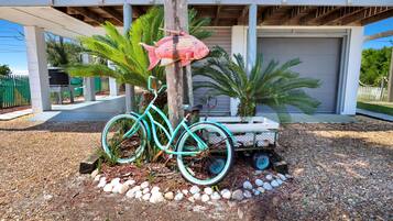 Uma bicicleta turquesa com decoração de peixe, uma palmeira e um carrinho branco com uma figura de peixe.