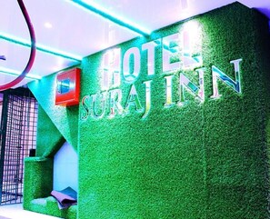 Placa do Hotel Suraj Inn, com parede texturizada verde e caixa de correio vermelha.