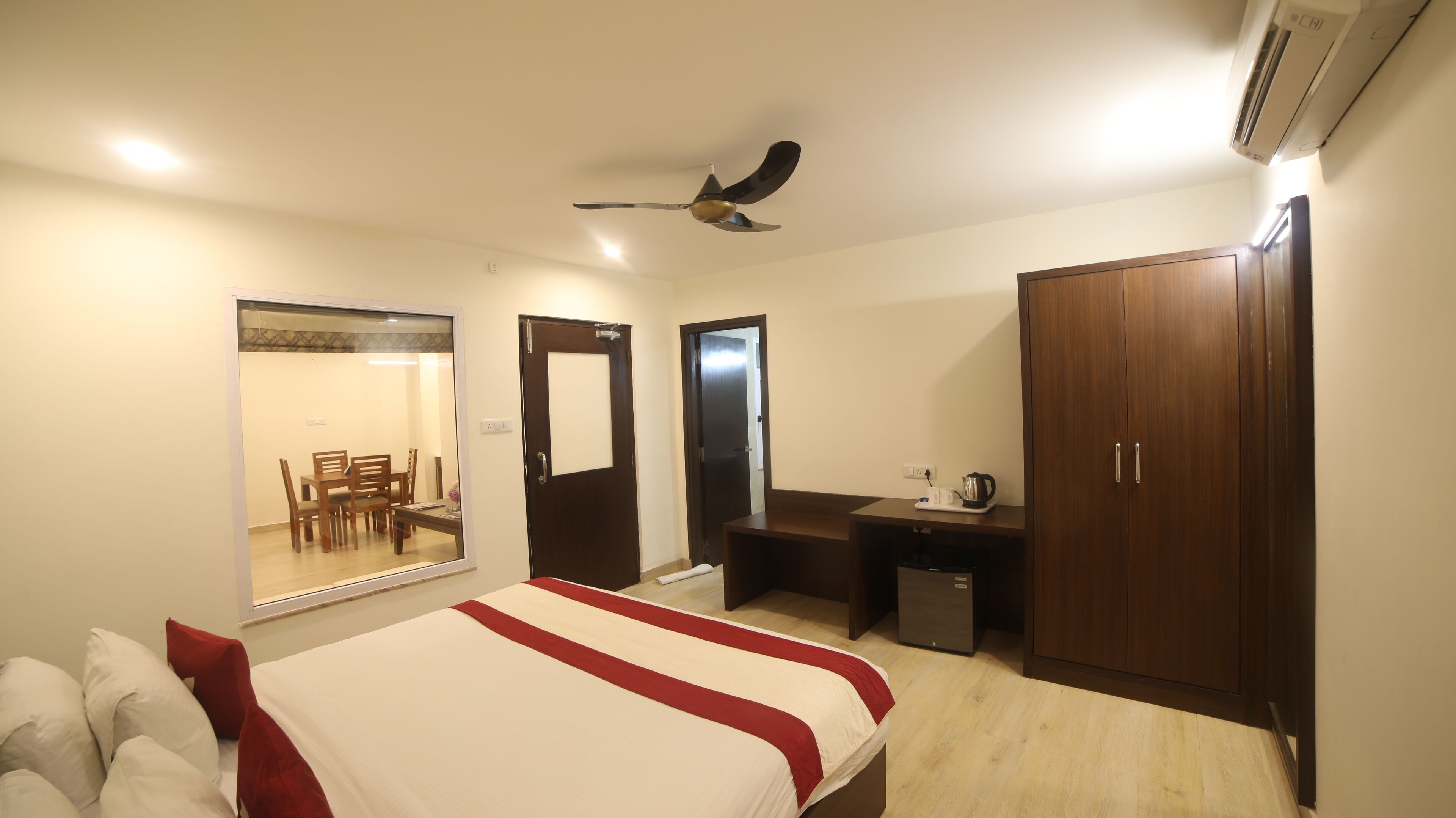 Quarto de hotel com cama, escrivaninha, guarda-roupa, espelho e ventoinha no teto.