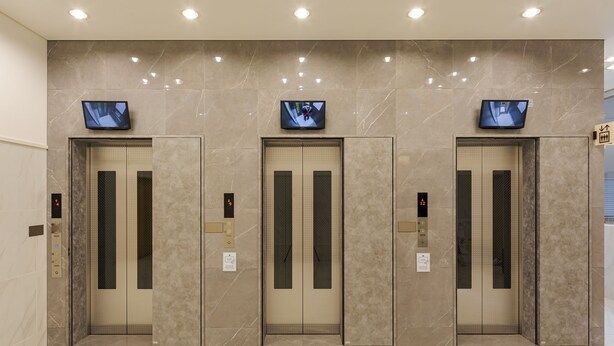 Três portas de elevador com mostradores digitais, uma parede de mármore e um chão ladrilhado.