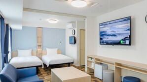 Quarto de hotel com duas camas, uma escrivaninha, uma cadeira, uma televisão e um relógio na parede.