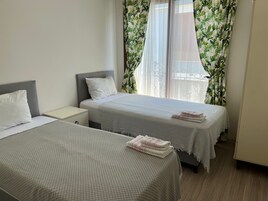 Quarto de hotel com duas camas, mesa de cabeceira, guarda-roupa e janela com cortinas florais.