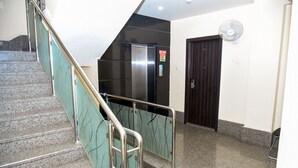 Uma escada com corrimãos de metal, um refrigerador, uma porta e um ventilador fixado na parede.