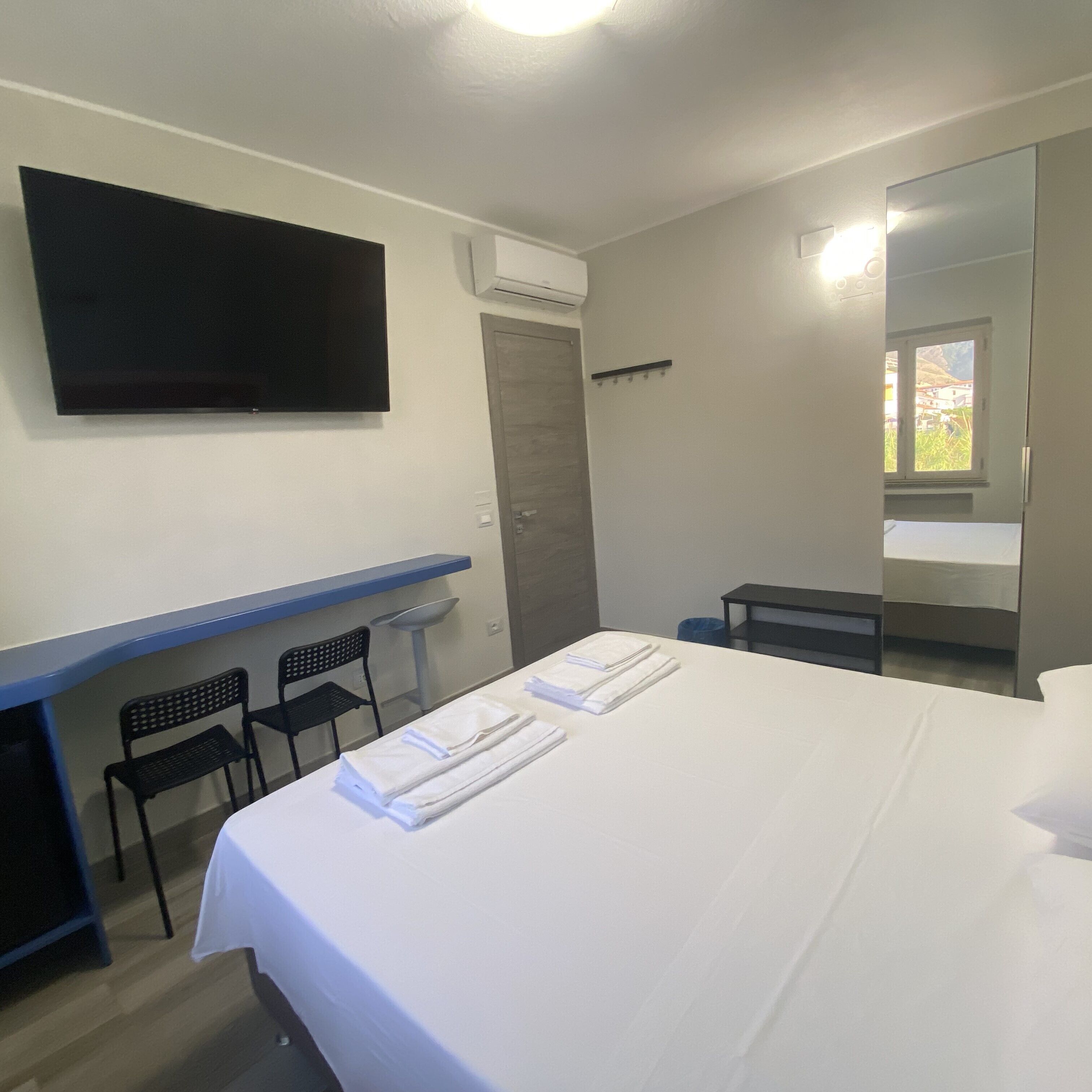 Quarto de hotel com cama, escrivaninha, cadeira, televisão de tela plana e janela com vista para edifícios.