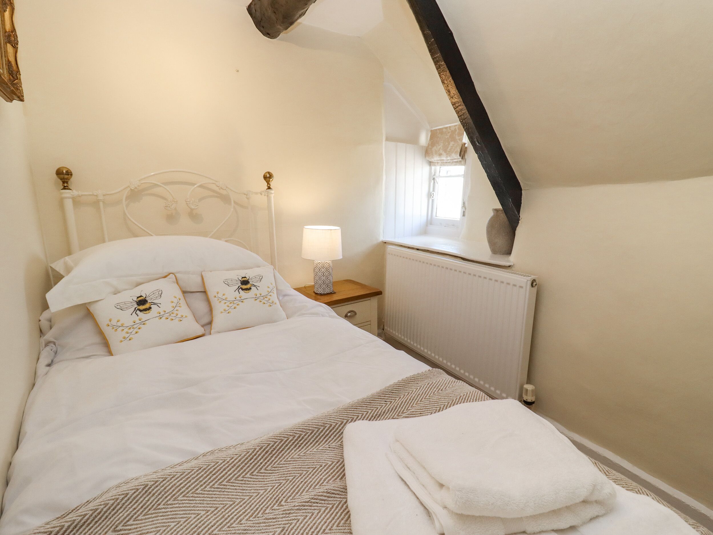 Uma cama bem arrumada com roupa de cama branca e almofadas decorativas, uma mesa de cabeceira com abajur e um radiador.