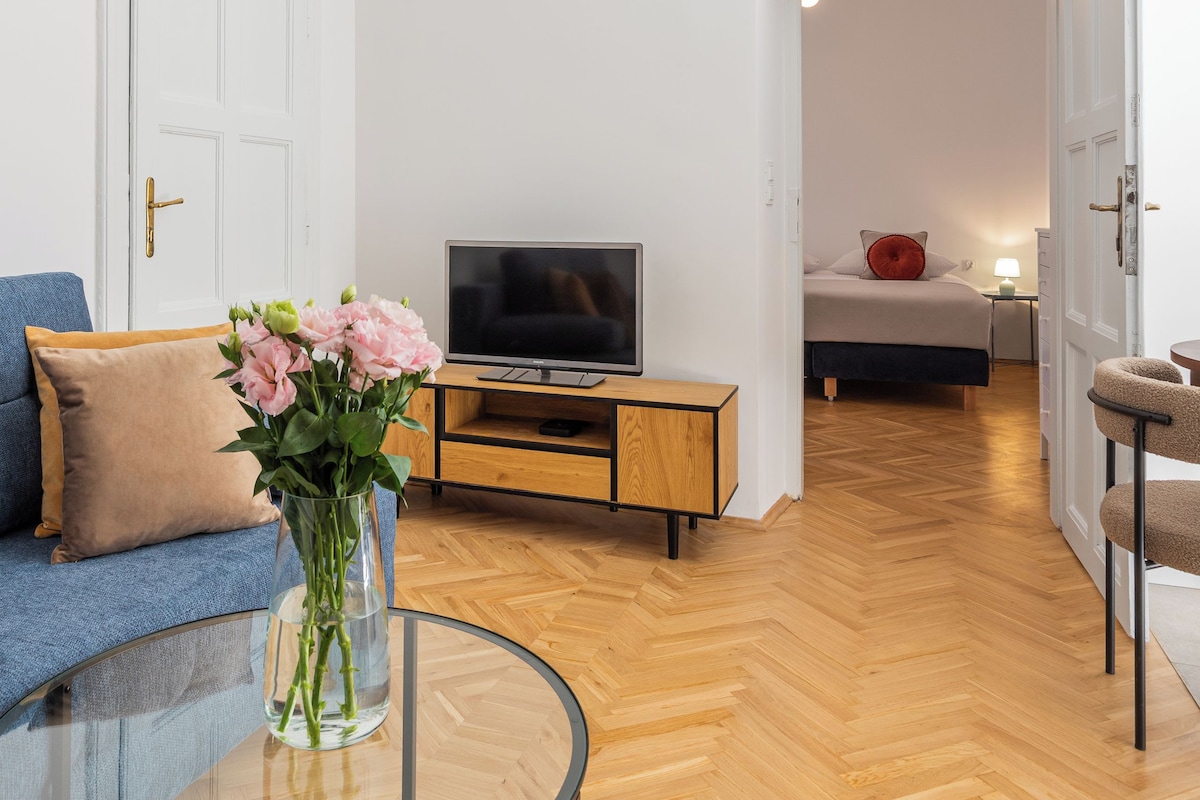 Sala de estar moderna com sofá, mesa de centro de vidro, televisão e piso de madeira.