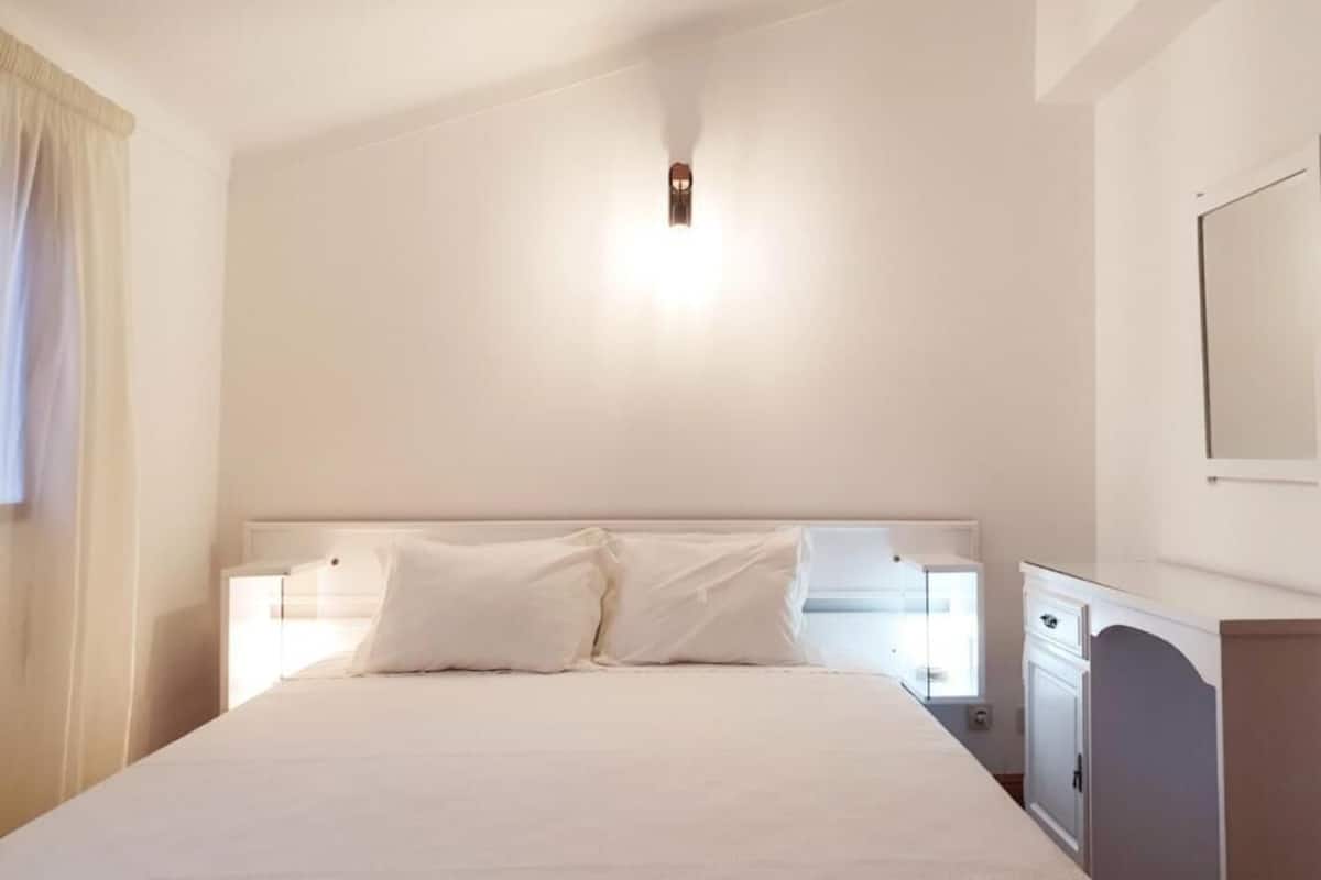 Quarto de hotel com uma cama de solteiro, mesa de cabeceira, guarda-roupa e espelho na parede.