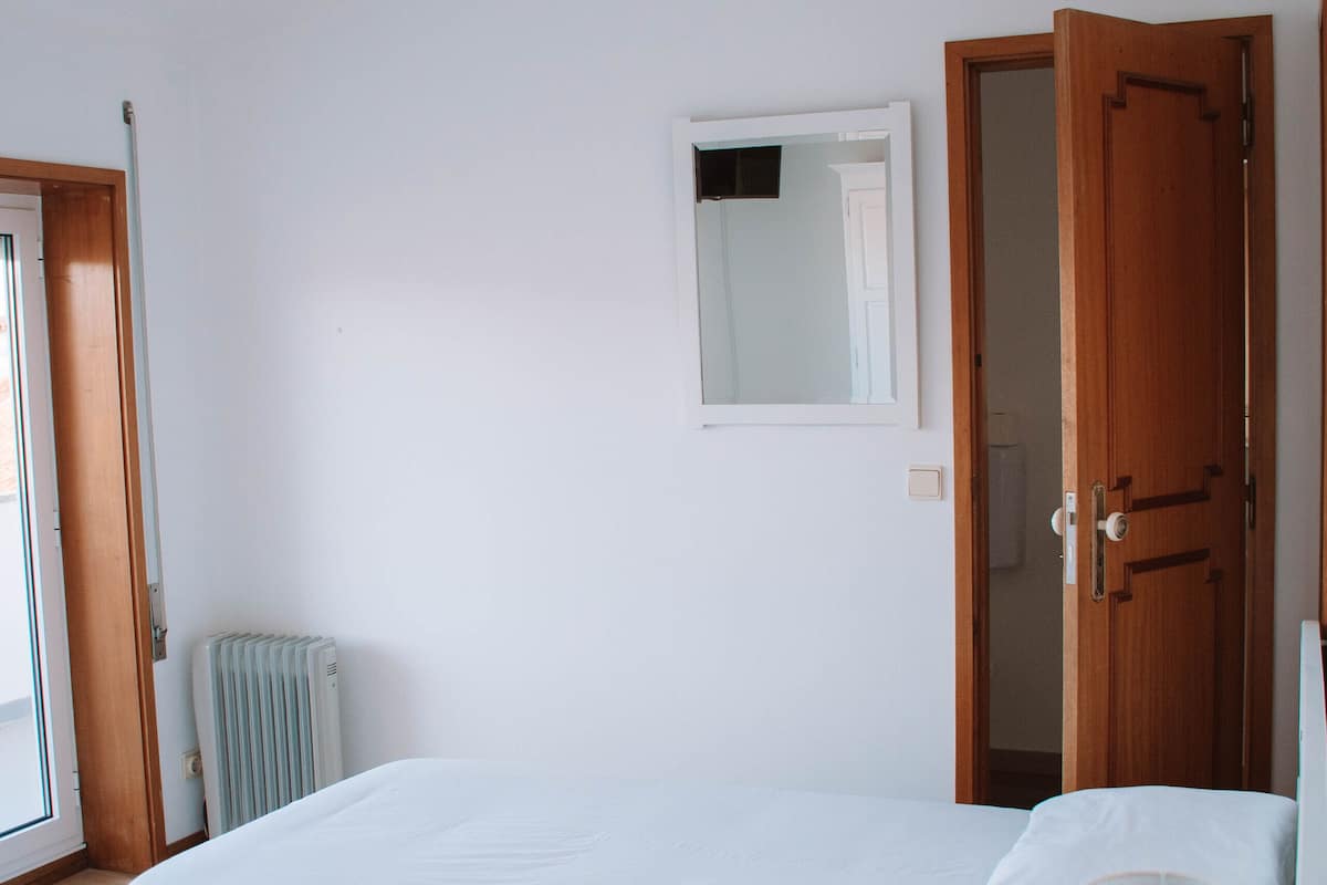 Quarto com duas camas, uma mesa de cabeceira com abajur, porta de madeira e radiador.