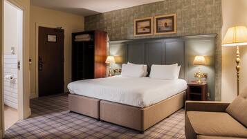 Quarto de hotel com uma cama grande, duas mesas de cabeceira com abajures, um guarda-roupa e um tapete xadrez.