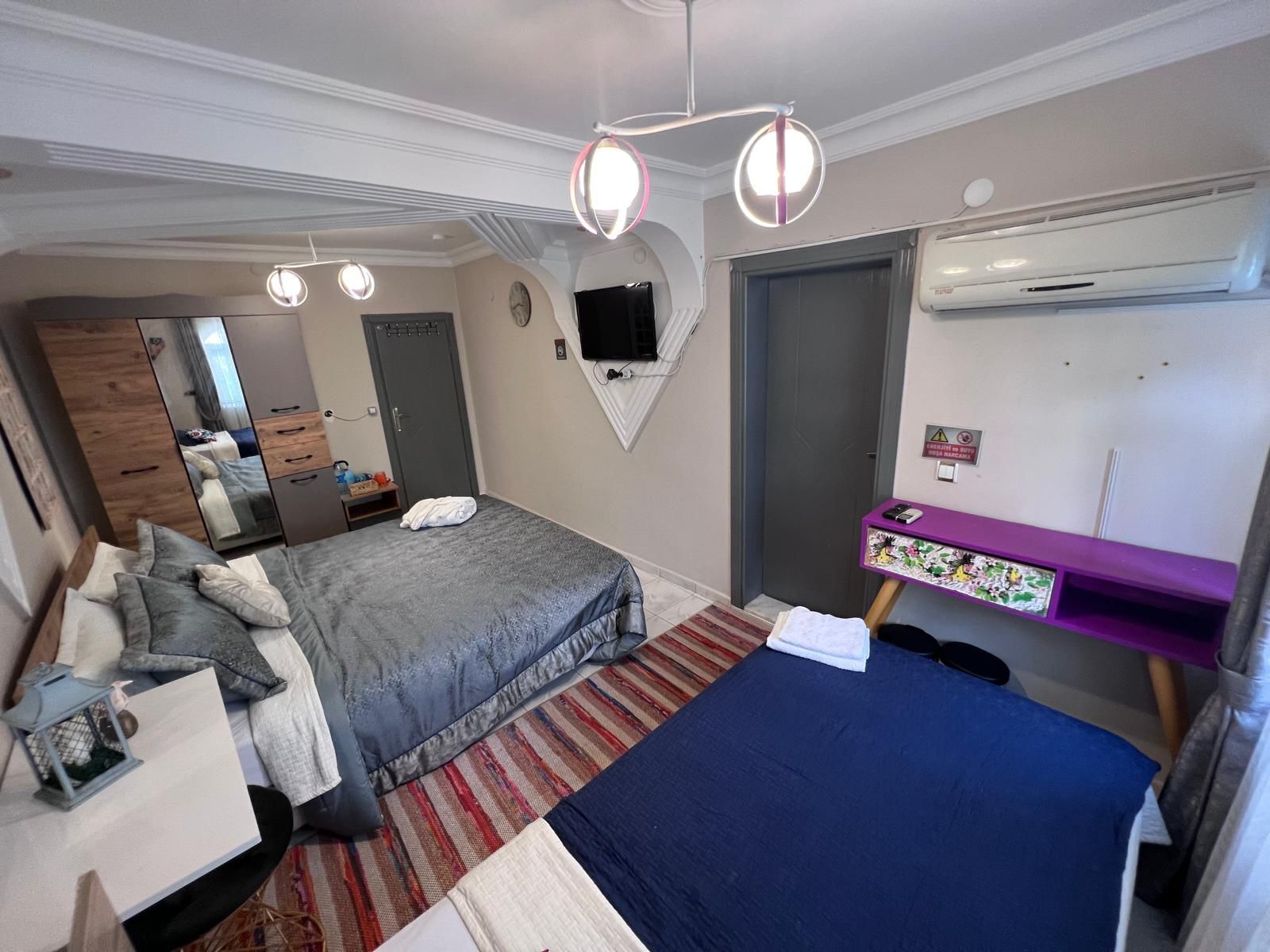 Quarto com cama, escrivaninha, espelho e televisão na parede.