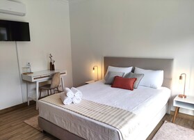 Quarto de hotel com cama, escrivaninha, cadeira, televisão e mesa de cabeceira com abajur.
