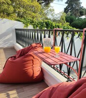 Varanda com mesa de metal vermelha, dois copos de suco de laranja e uma poltrona de feijão vermelho.