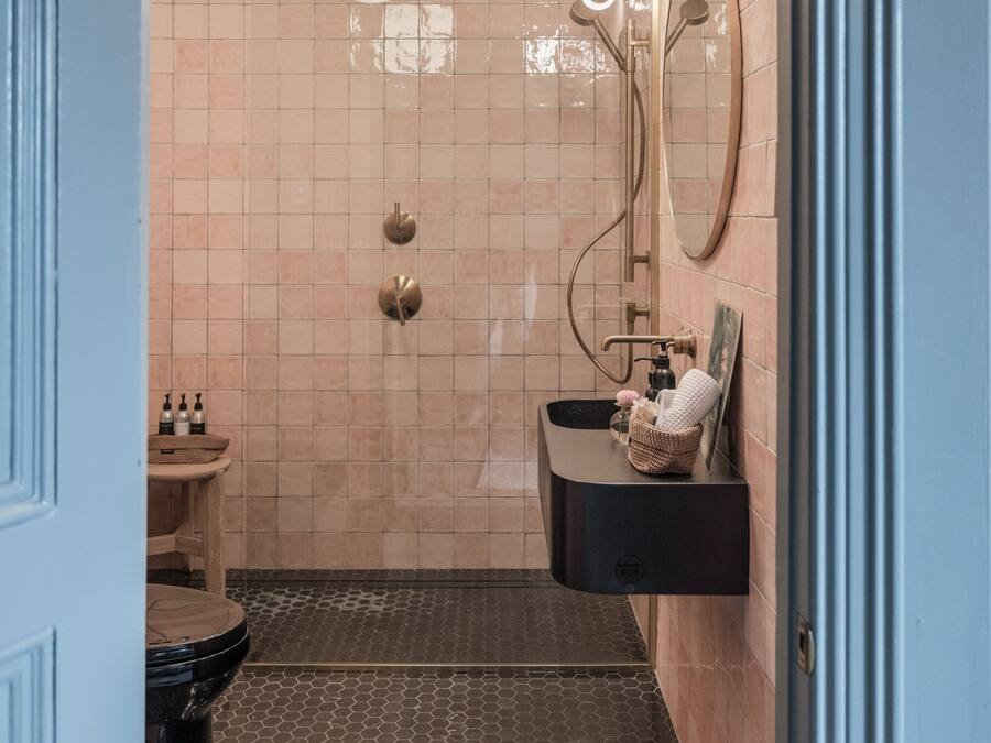 Casa de banho com chuveiro em mosaico, lavatório com espelho e candeeiro pendente.
