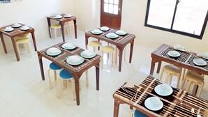 Uma sala de jantar com várias mesas preparadas para refeições, uma porta de madeira e uma janela com vista.
